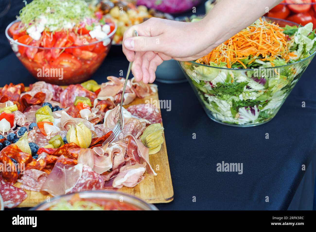 Hand takes meat snacks from meat platter on the buffet table during a ...