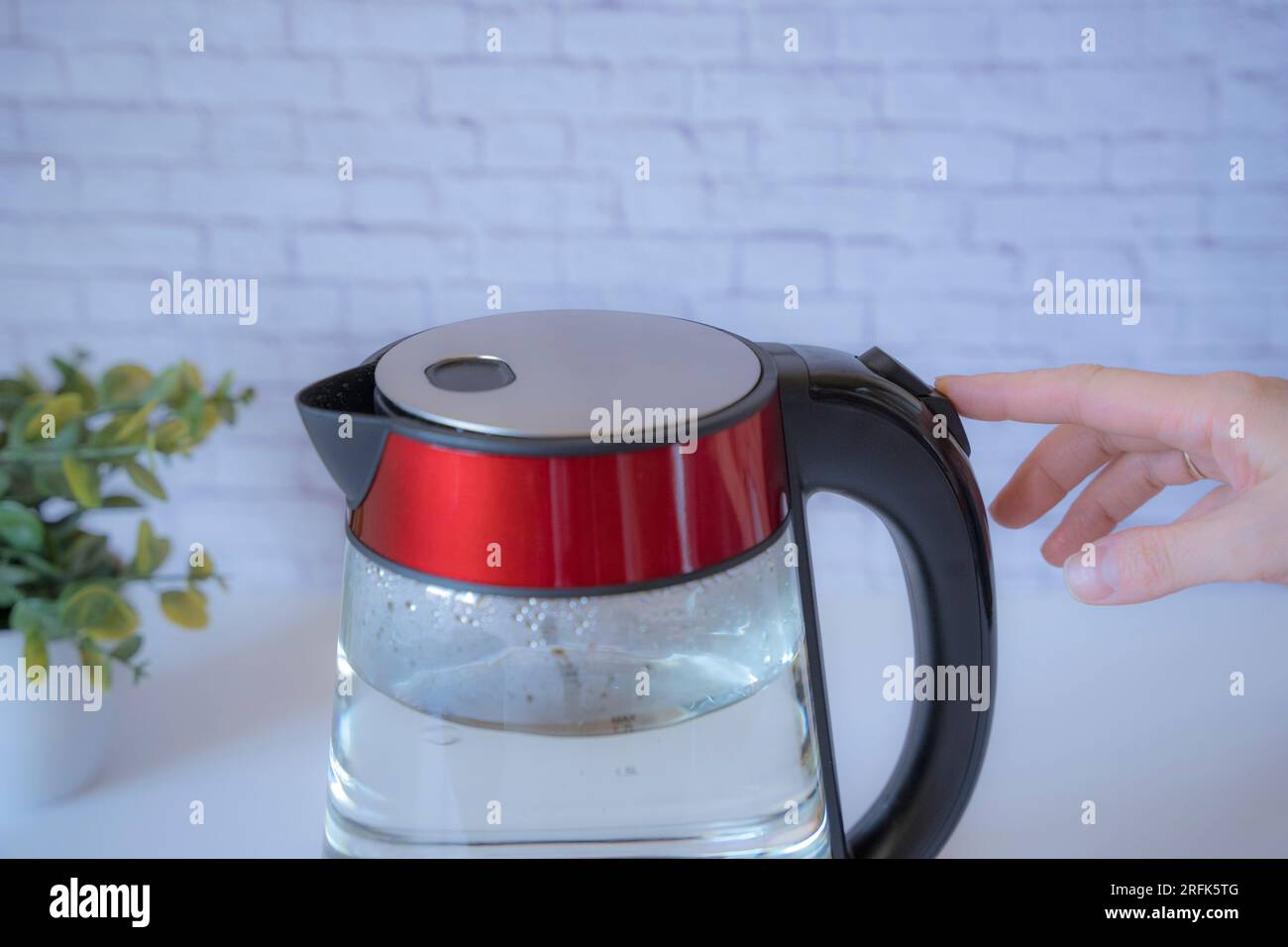a modern electric kettle with boiling water and a a woman's hand ...