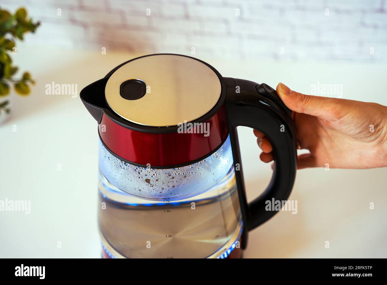 a modern electric kettle with boiling water and a a woman's hand ...