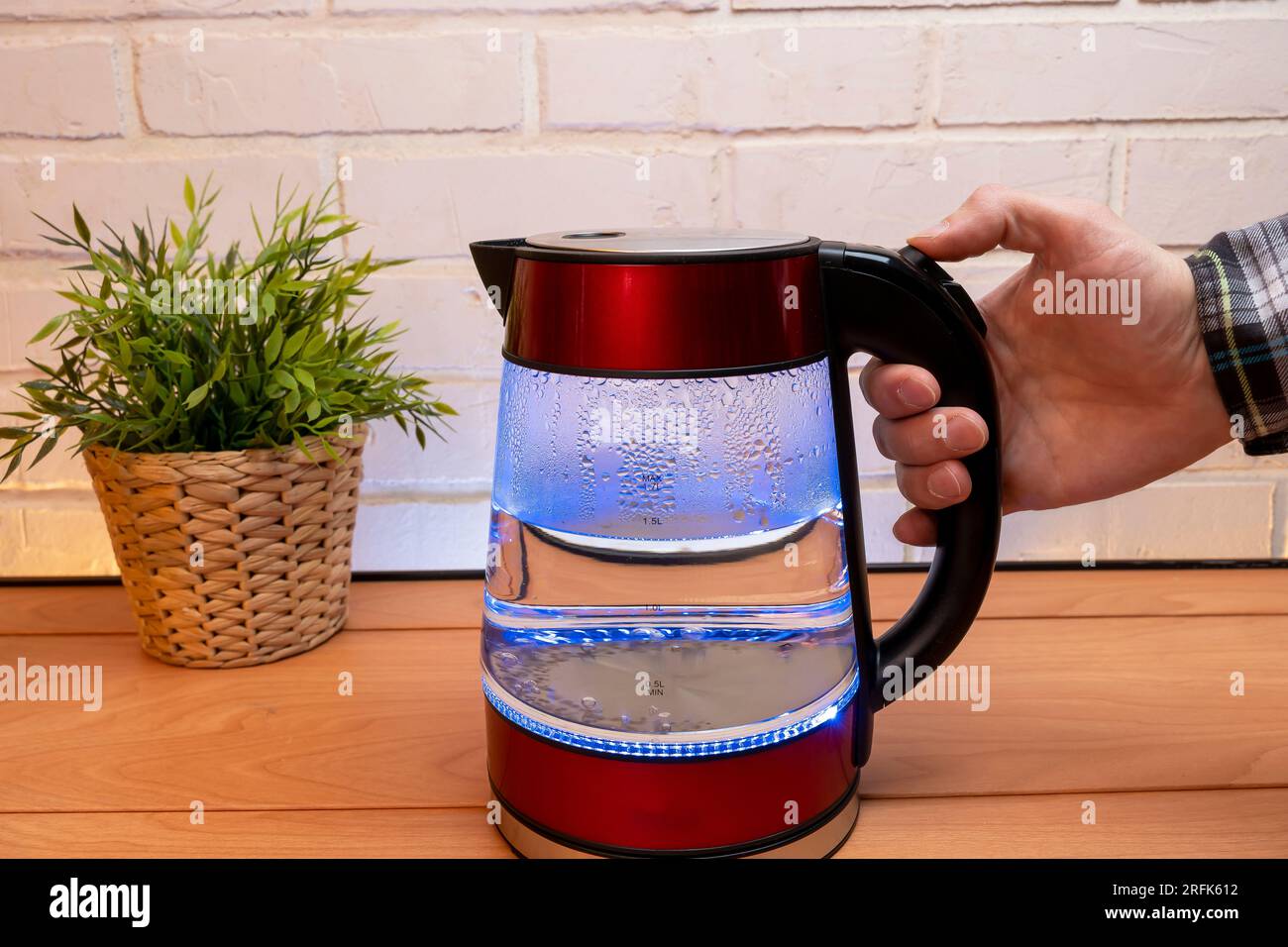 an electric kettle in neon blue light and a man's hand pressing the off ...