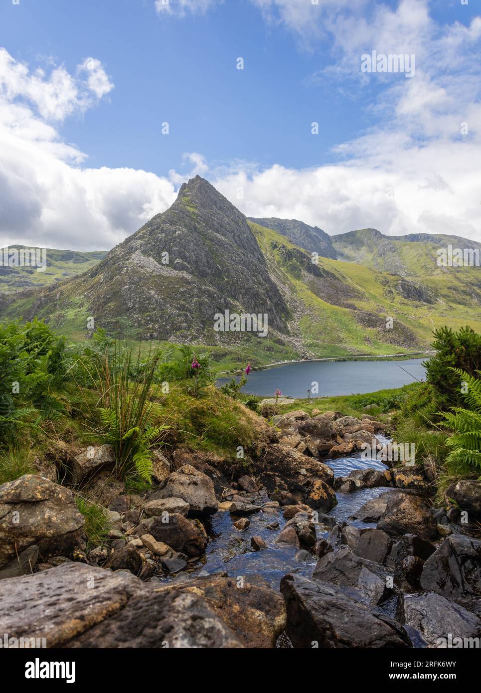 View of pyramid shaped mountain. Stream in foreground. Blue sky and ...