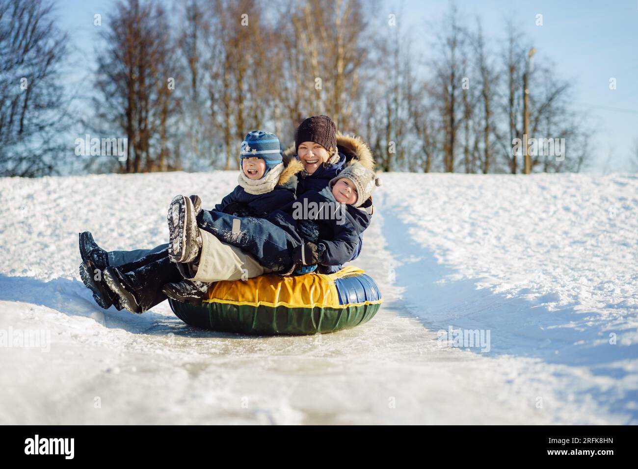 Young caucasian pretty woman with two cute boys sledding down the icy ...
