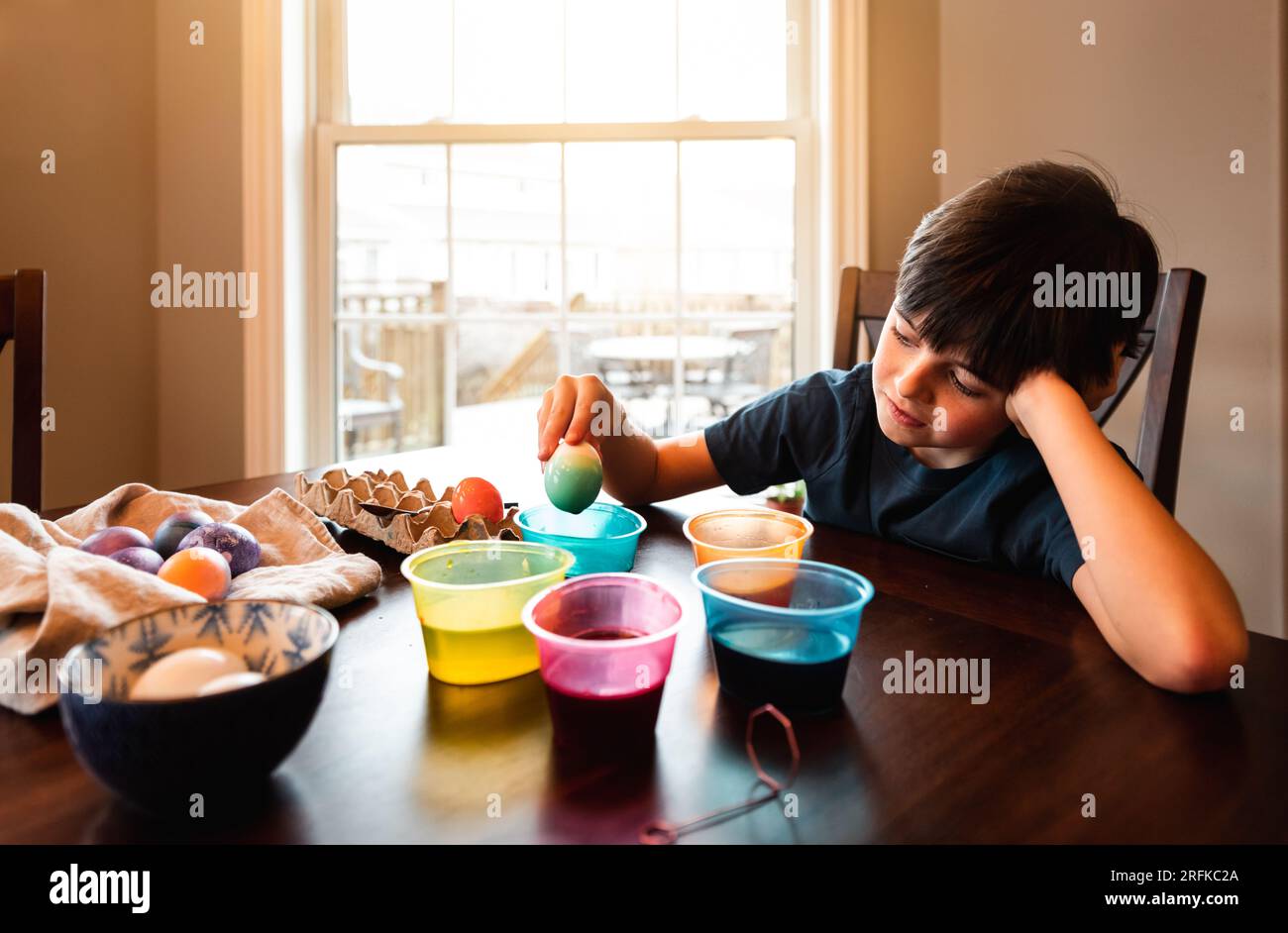 Young boy coloring easter eggs with containers of dye at the table ...