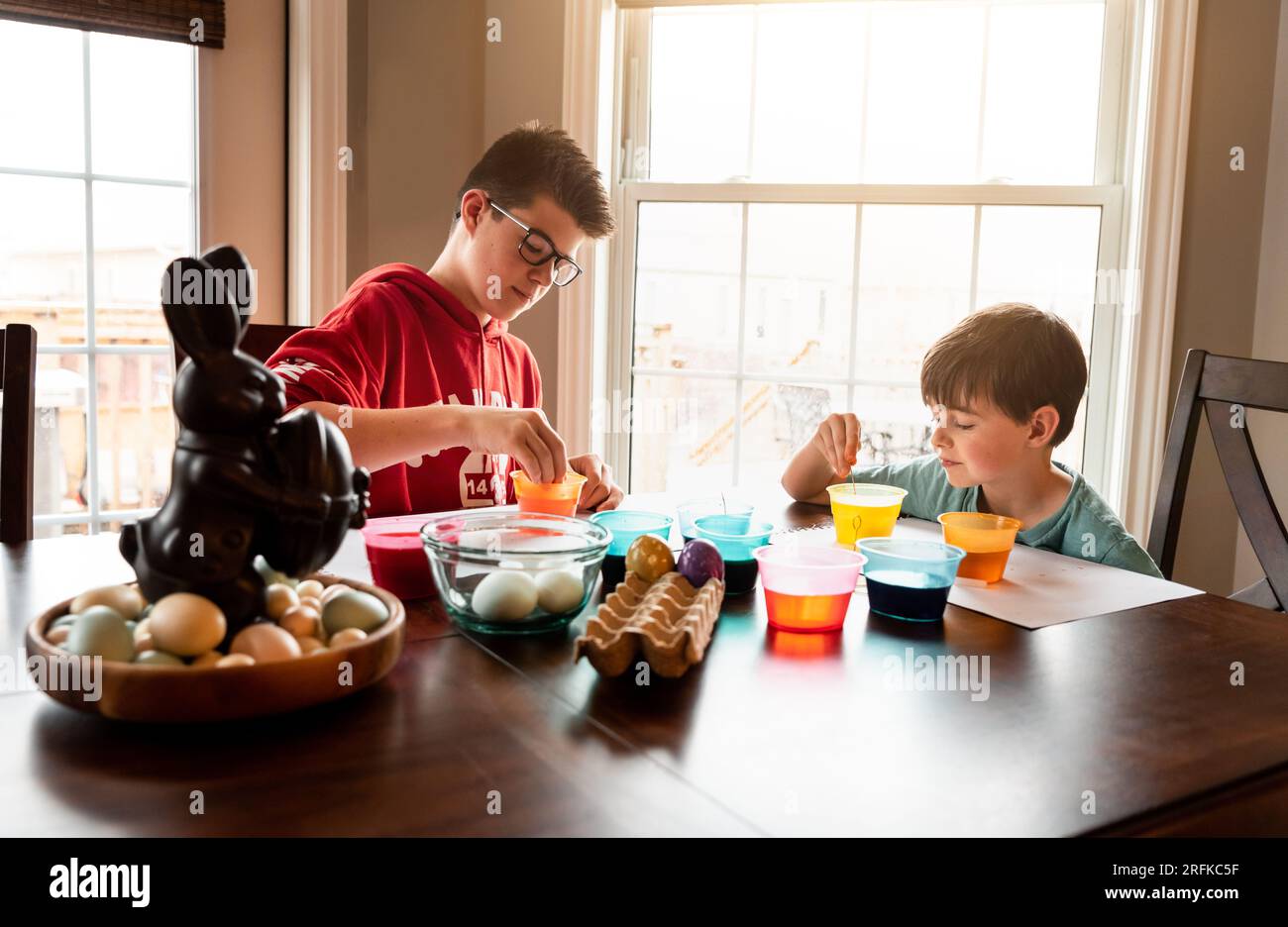 Two boys coloring easter eggs with containers of dye at wooden table ...
