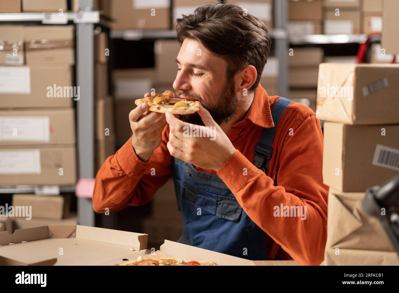 Young warehouse worker eating pizza at lunch at workplace, food at work ...