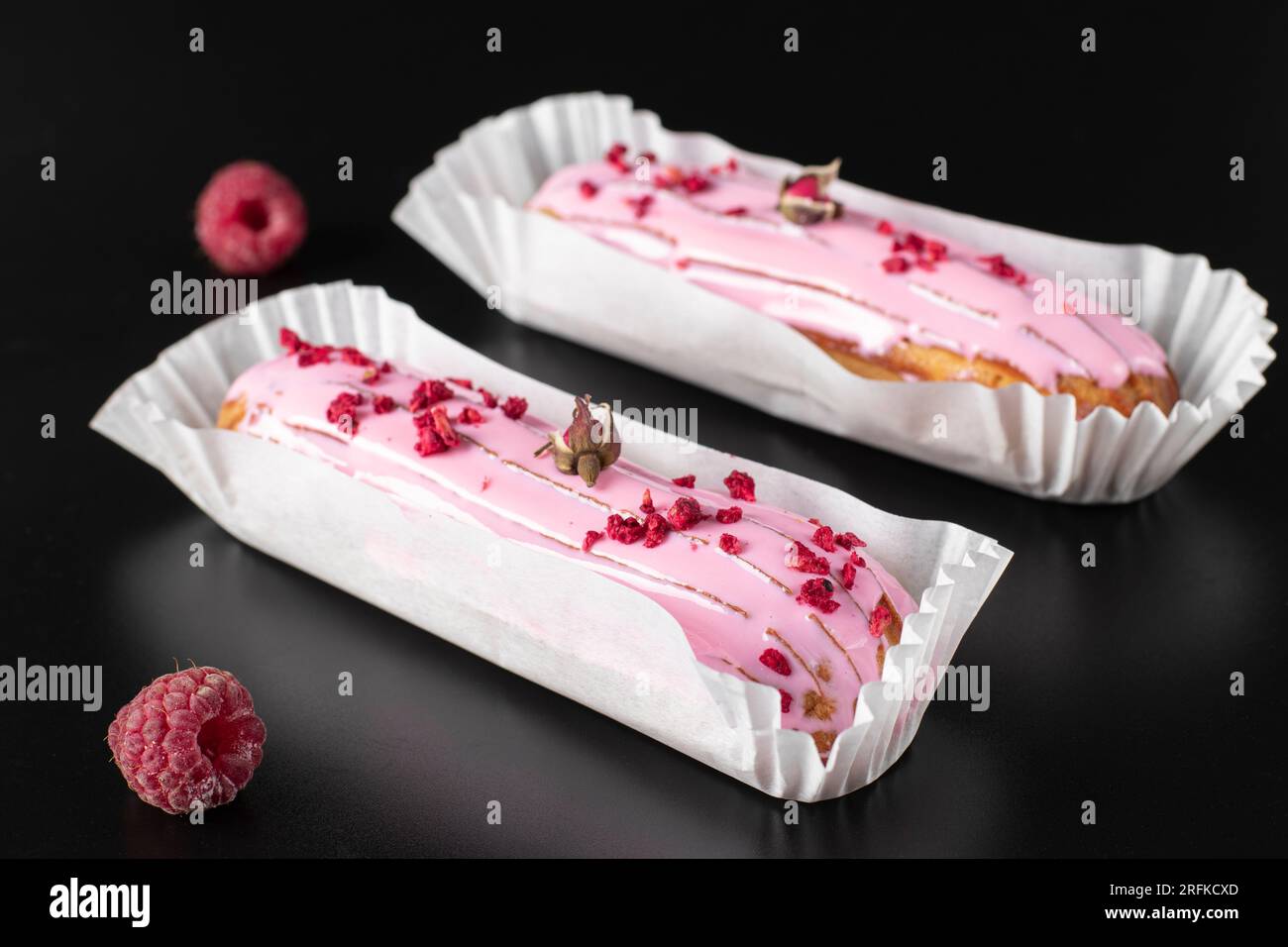 Berry eclairs covered with pink icing and decorated with flowers on a ...