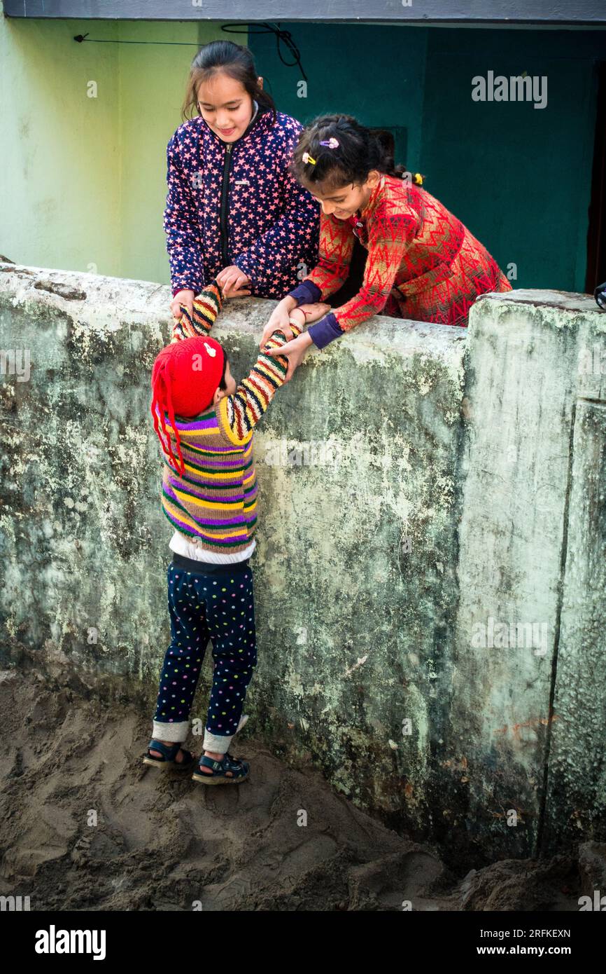 Oct.14th 2022 Uttarakhand, India. Young sisters playfully pulling their baby brother up a wall ...