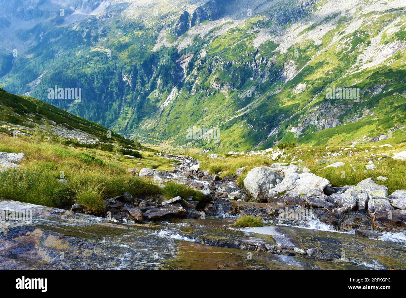Stream of water flowing down a steep slope into a alpine valley in High ...