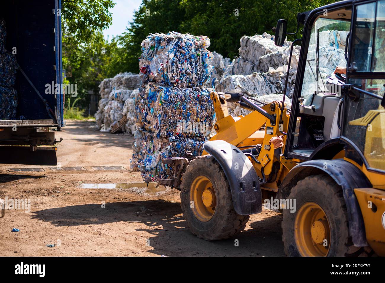 Excavator carrying cubes of compressed plastic garbage to a truck at ...