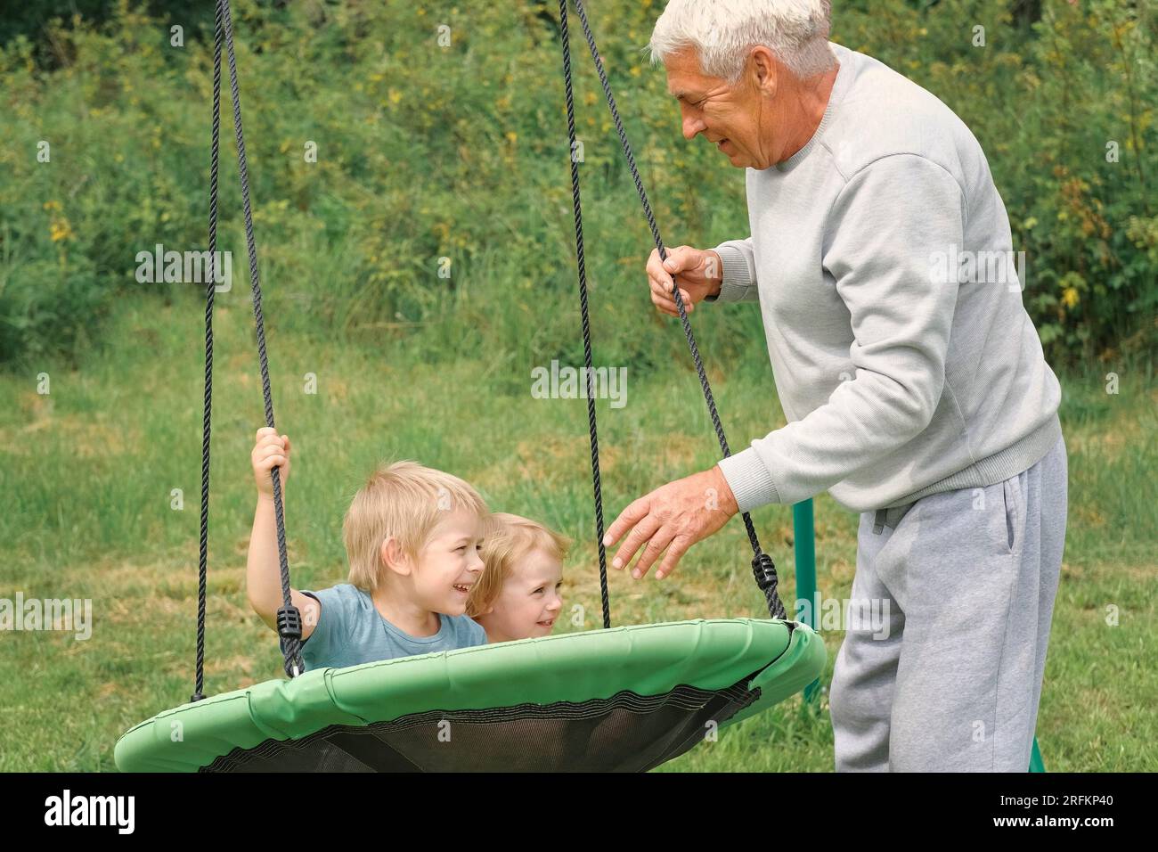 Grandfather swinging children in summer park. Grand dad and ...