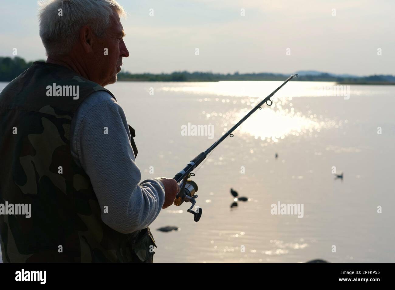 Old man fishing. Senior gray haired fisherman throws a spinning from ...