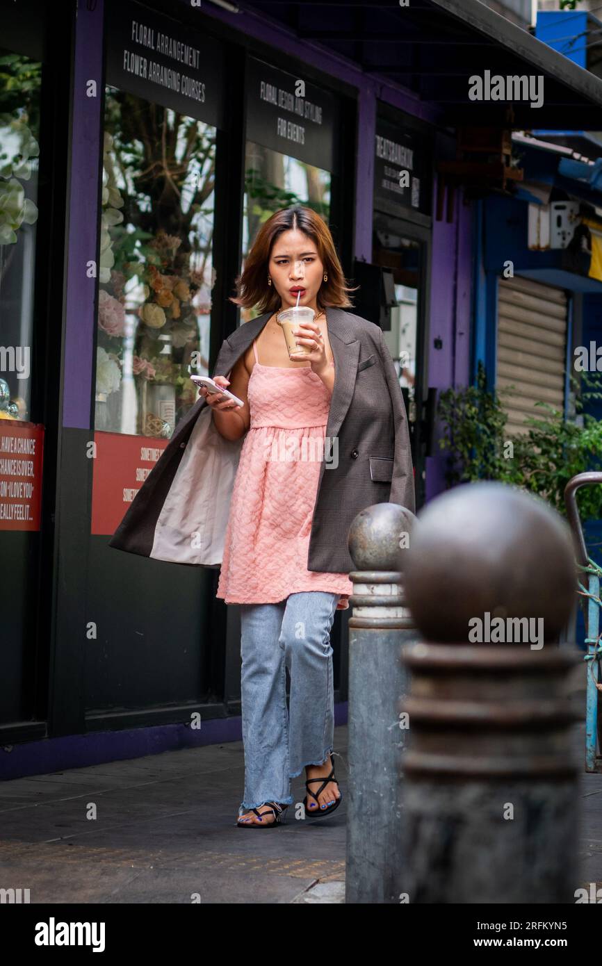 A young Thai girl sips her coffee and checks her phone making her way ...