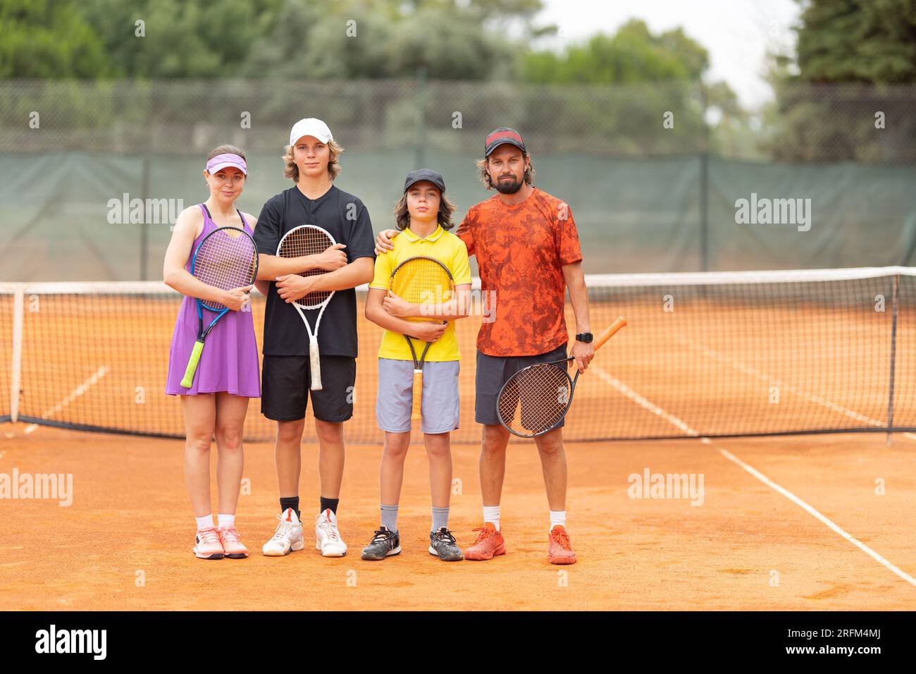 A family of mother and father and their two sons stand on a tennis ...
