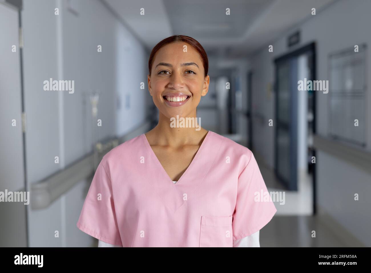 Portrait of happy biracial female doctor wearing scrubs in corridor at ...