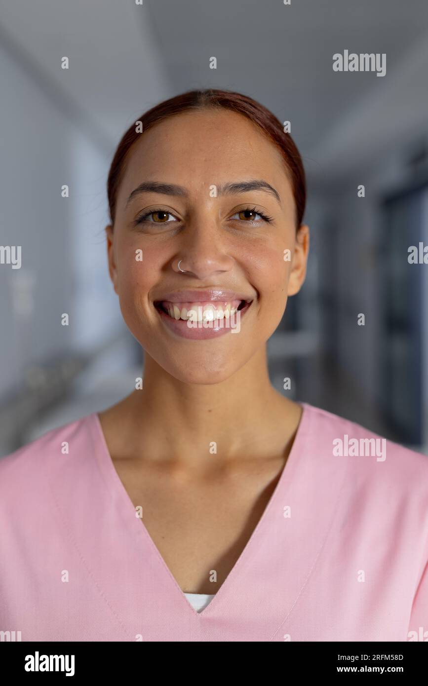 Portrait of happy biracial female doctor wearing scrubs in corridor at ...