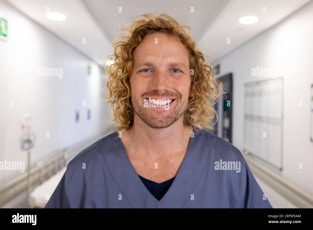 Portrait of happy caucasian male doctor wearing scrubs in corridor at ...