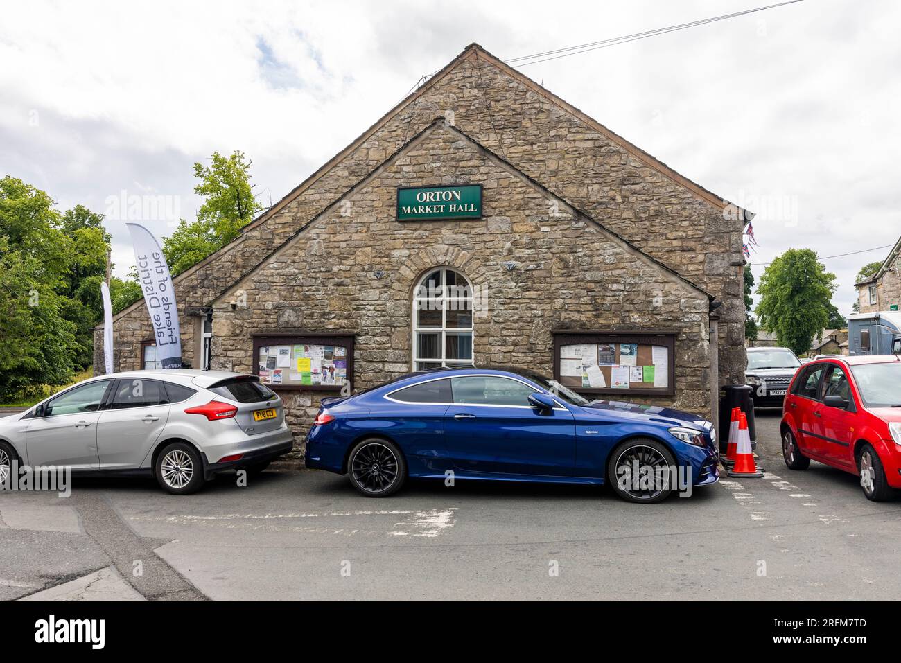 An overcast July days and cars are parked around the Orton Market Hall ...