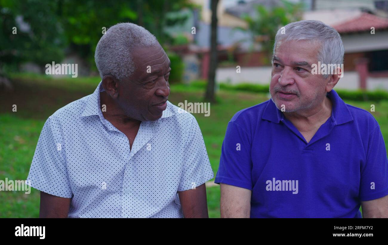 Two older diverse friends conversing at park bench. A retired African ...