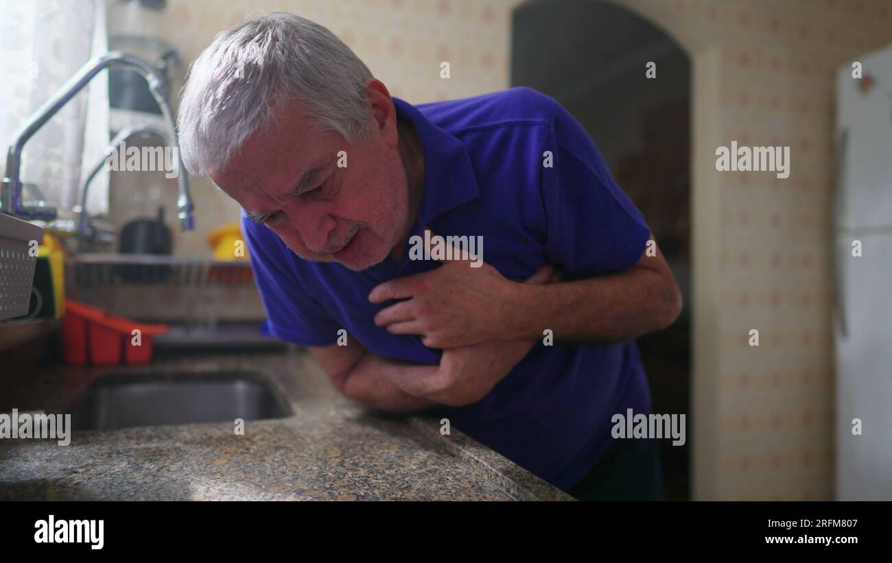 Senior man suffering heart attack alone at home leaning on kitchen sink ...