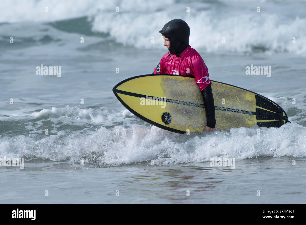 A young male surfer carrying his surfboard and walking out of the sea ...