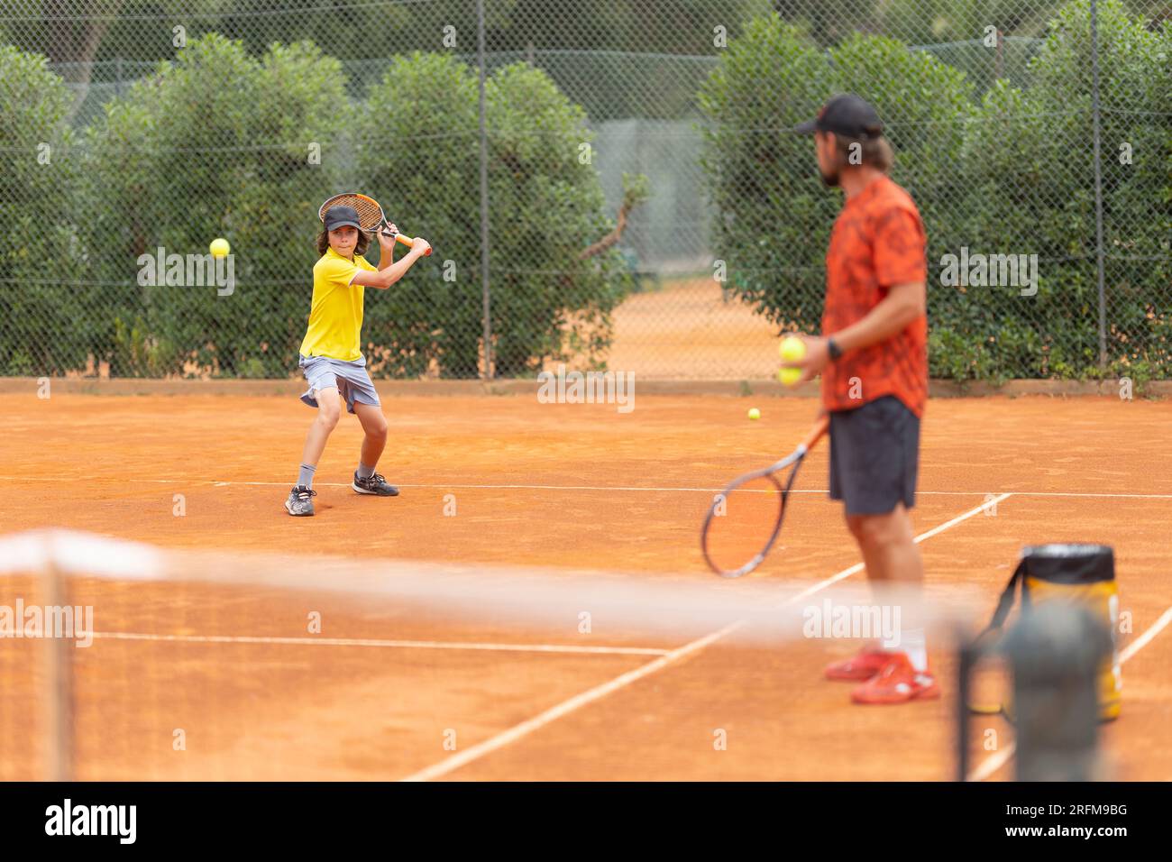 A father watches his son play tennis standing on the court. Mid shot ...