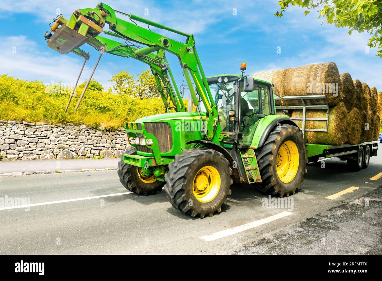 Traditional irish farming tractor with hay on public road at sunny day ...