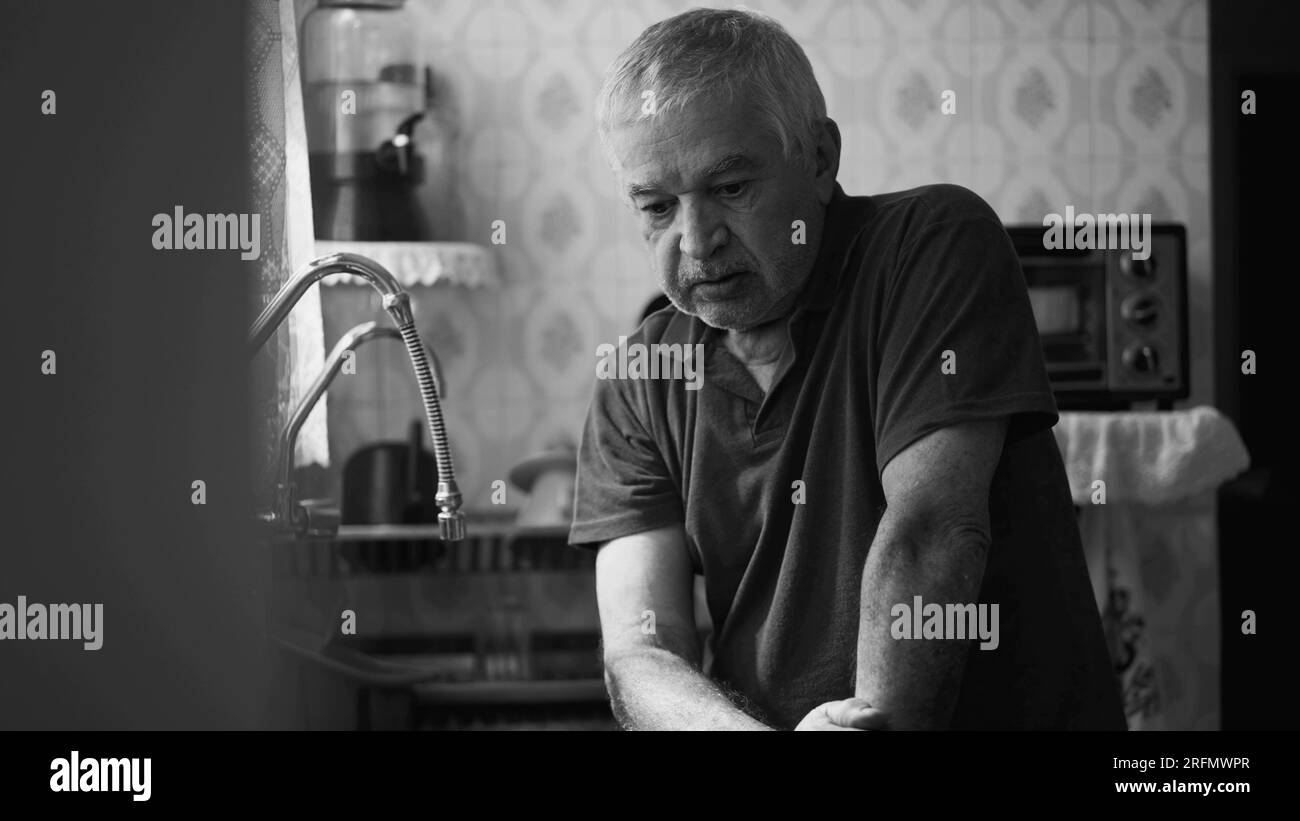 Senior man suffering from depression at home alone leaning by kitchen ...
