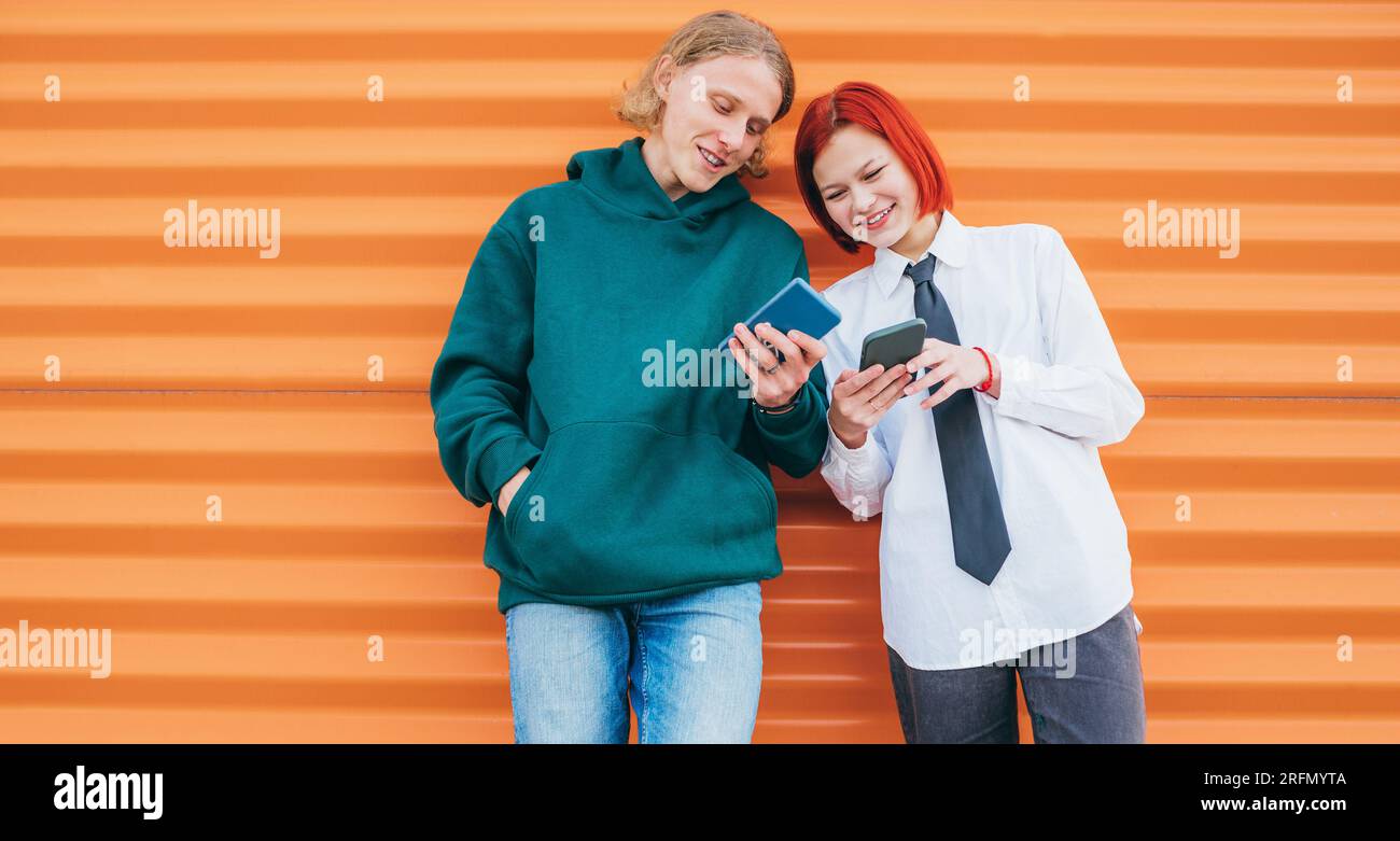 Two caucasian teen friends boy and a girl browsing their smartphone ...