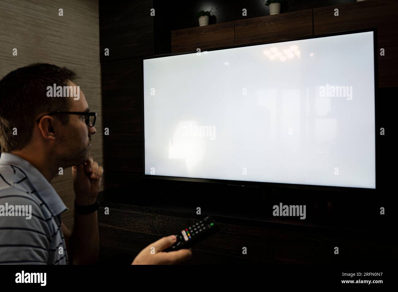 Man watching television, turning on plasma flatscreen TV-set, pointing remote control at empty ...
