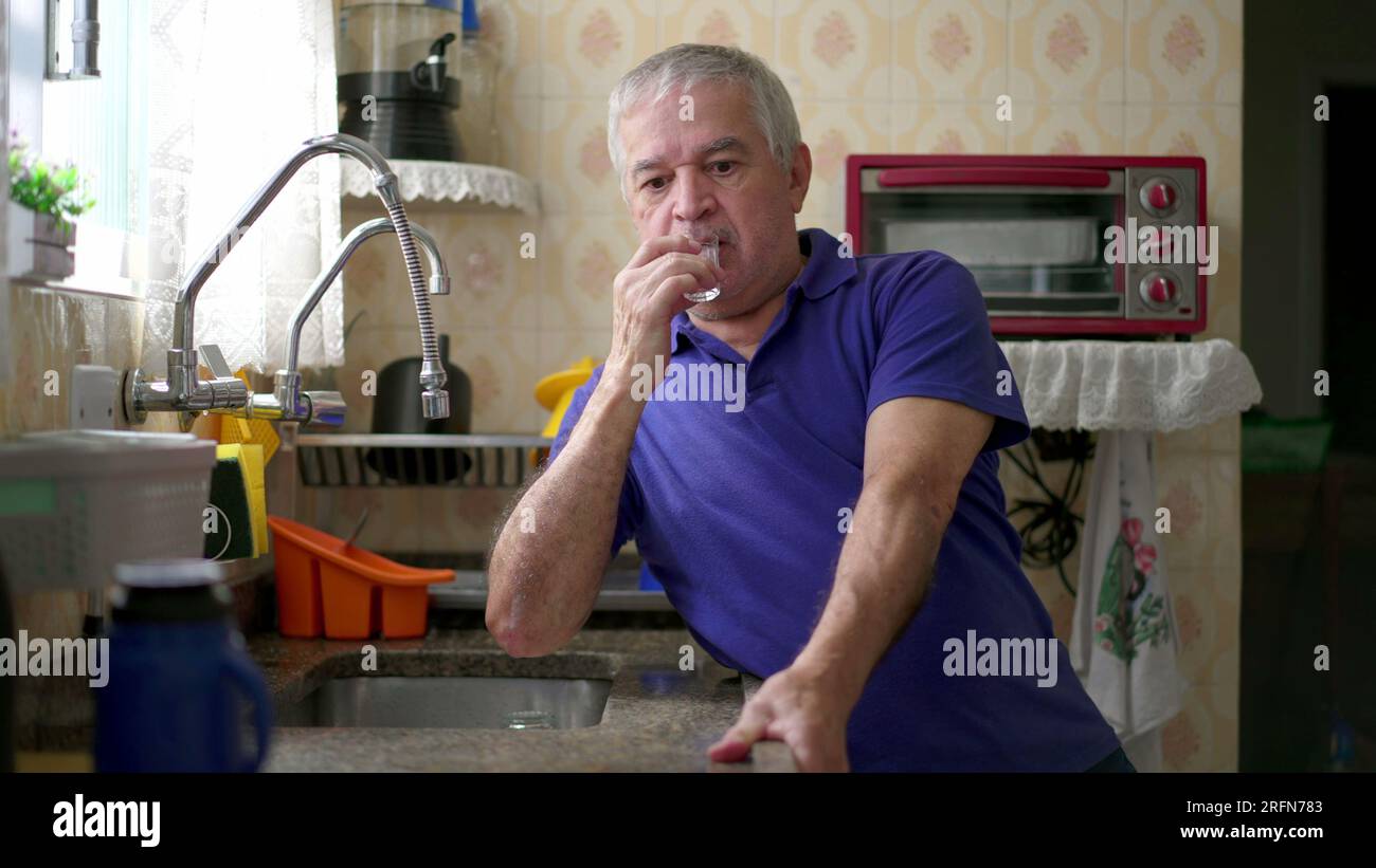 Drunk senior struggling with alcoholism leaning on kitchen sink at home ...