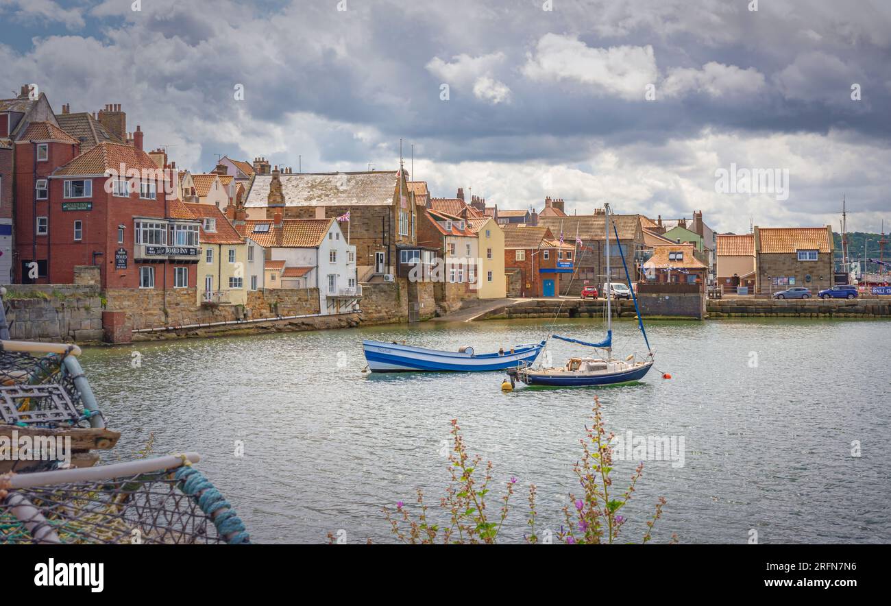 Two boats lie in harbour. Buildings line the waterfront and a quay is ...
