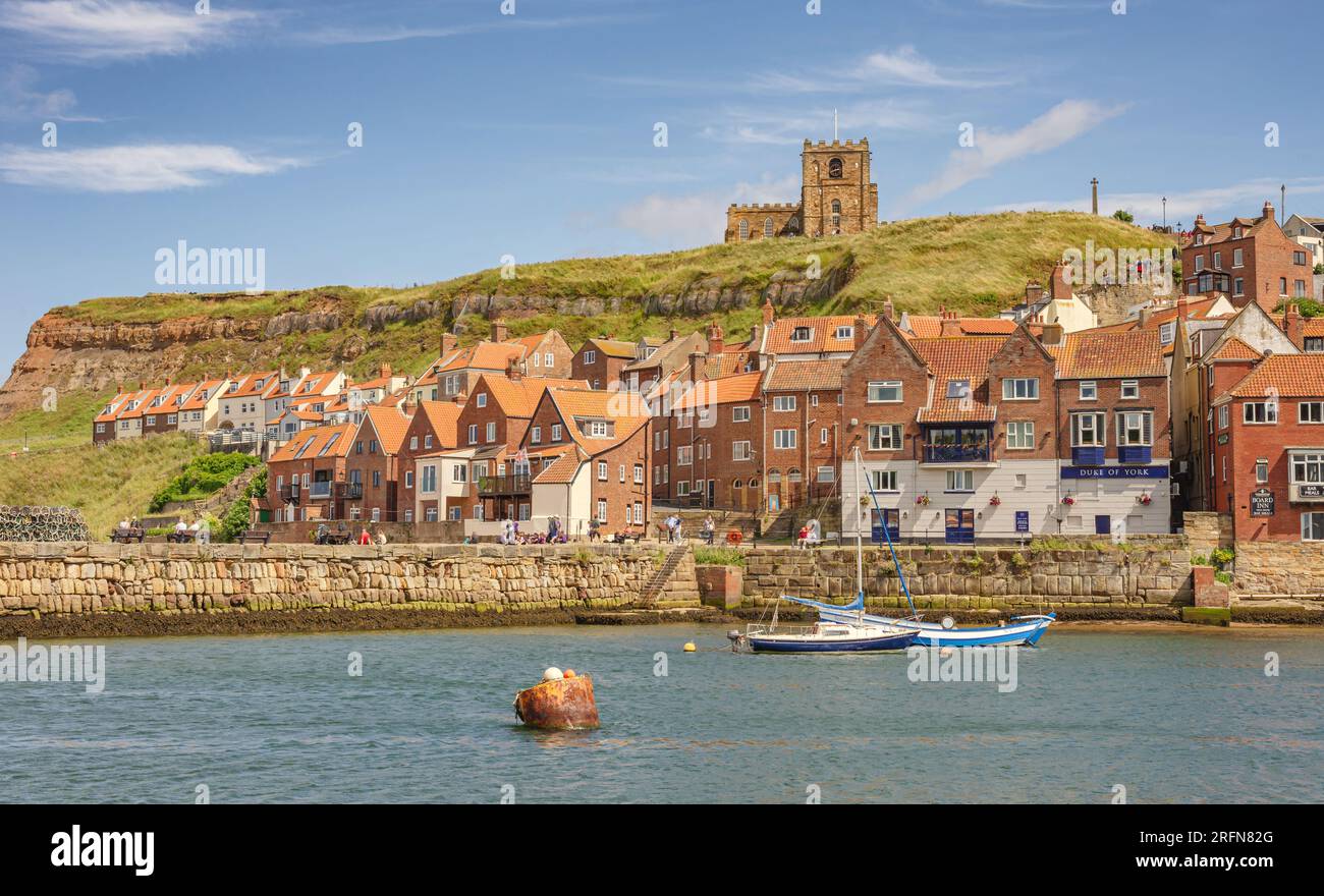 Two boats lie in harbour. Buildings line the waterfront and a quay is ...