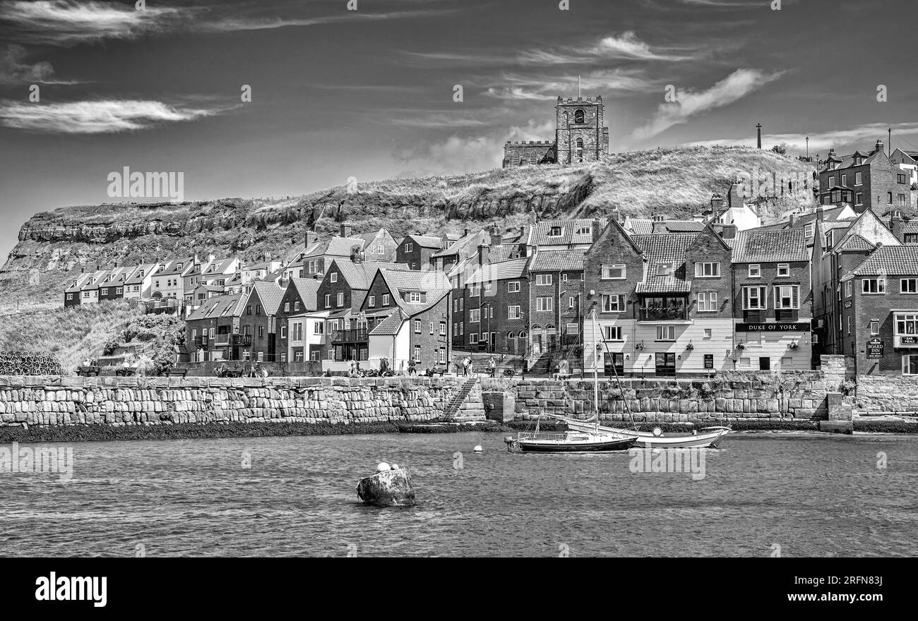 Two boats lie in harbour. Buildings line the waterfront and a quay is ...