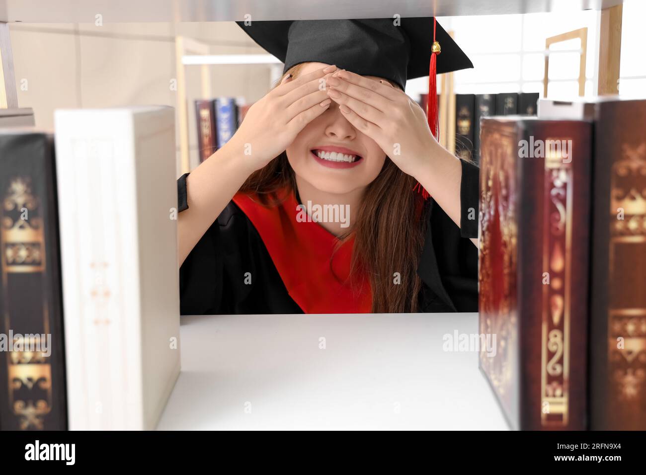 Female graduate student covering her eyes with hands near bookshelf in ...