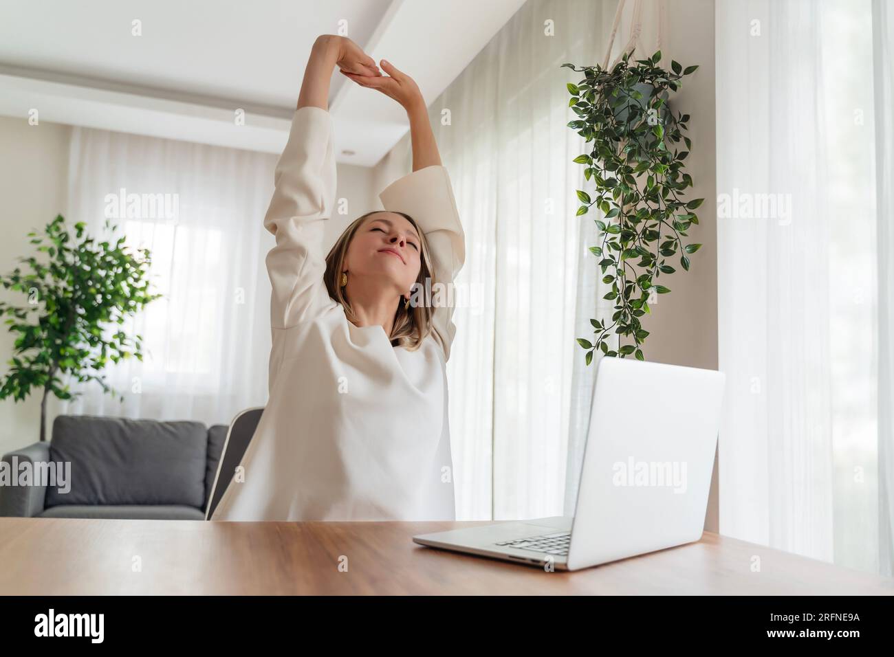 A young satisfied woman reaches her hands up and smiles while working ...