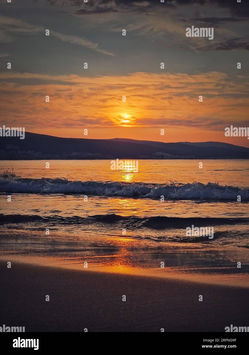 Early morning at the beach with vibrant sunrise at horizon and foamy ...