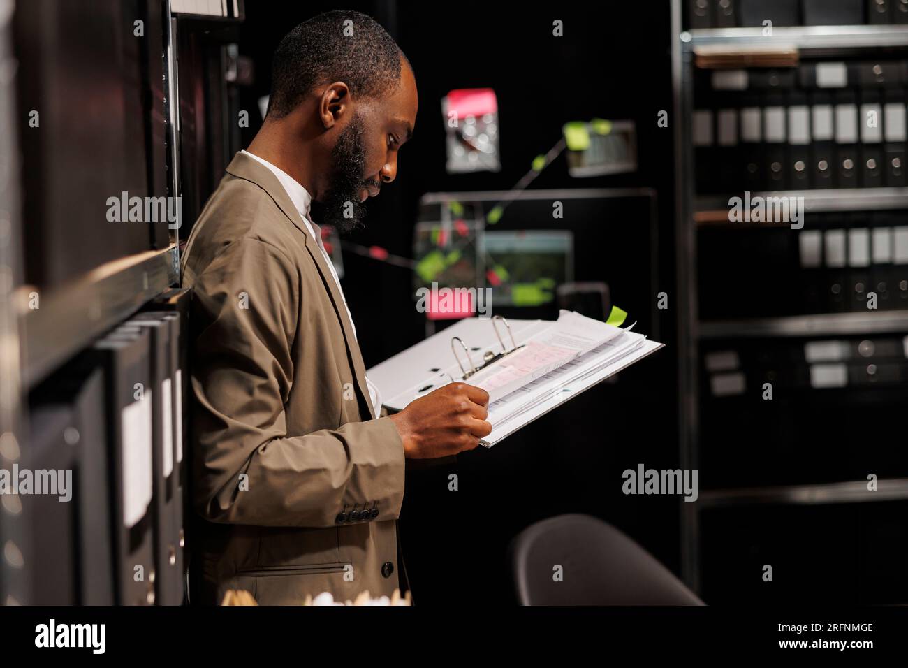 African american detective standing near shelf wit folders, reading ...