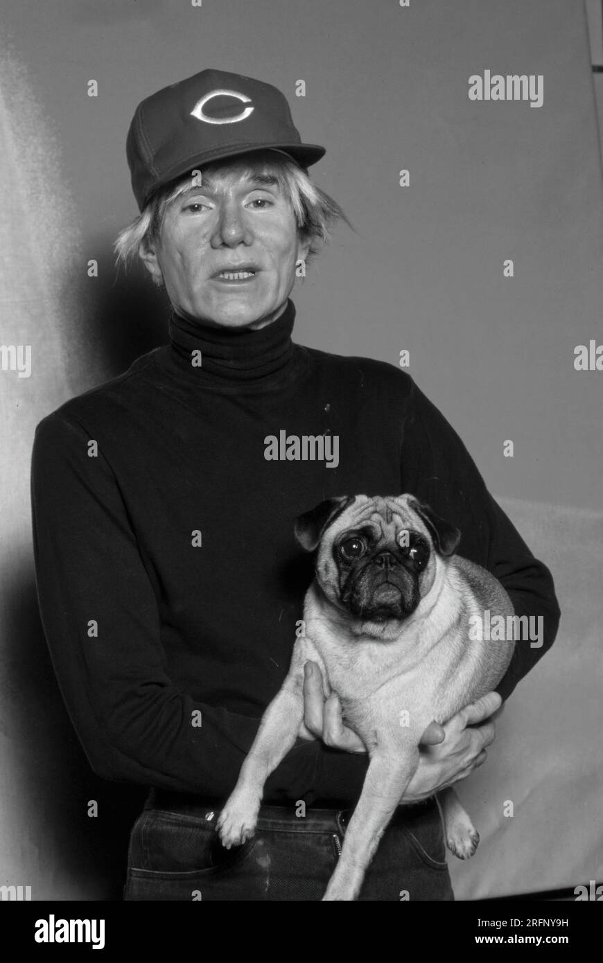 Andy Warhol poses wearing Cincinnati Reds baseball cap while holding ...