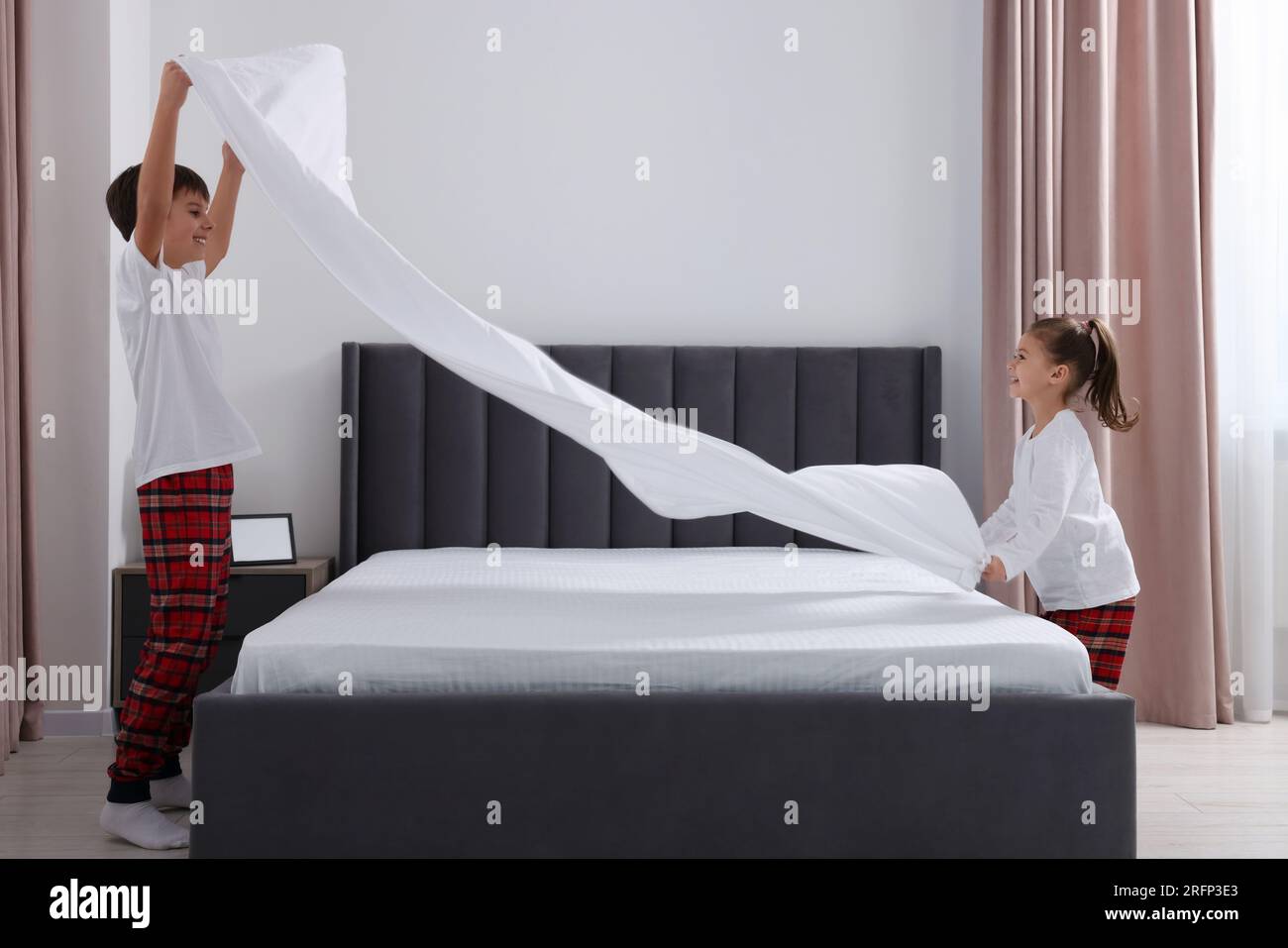 Brother and sister changing bed linens together in bedroom Stock Photo ...