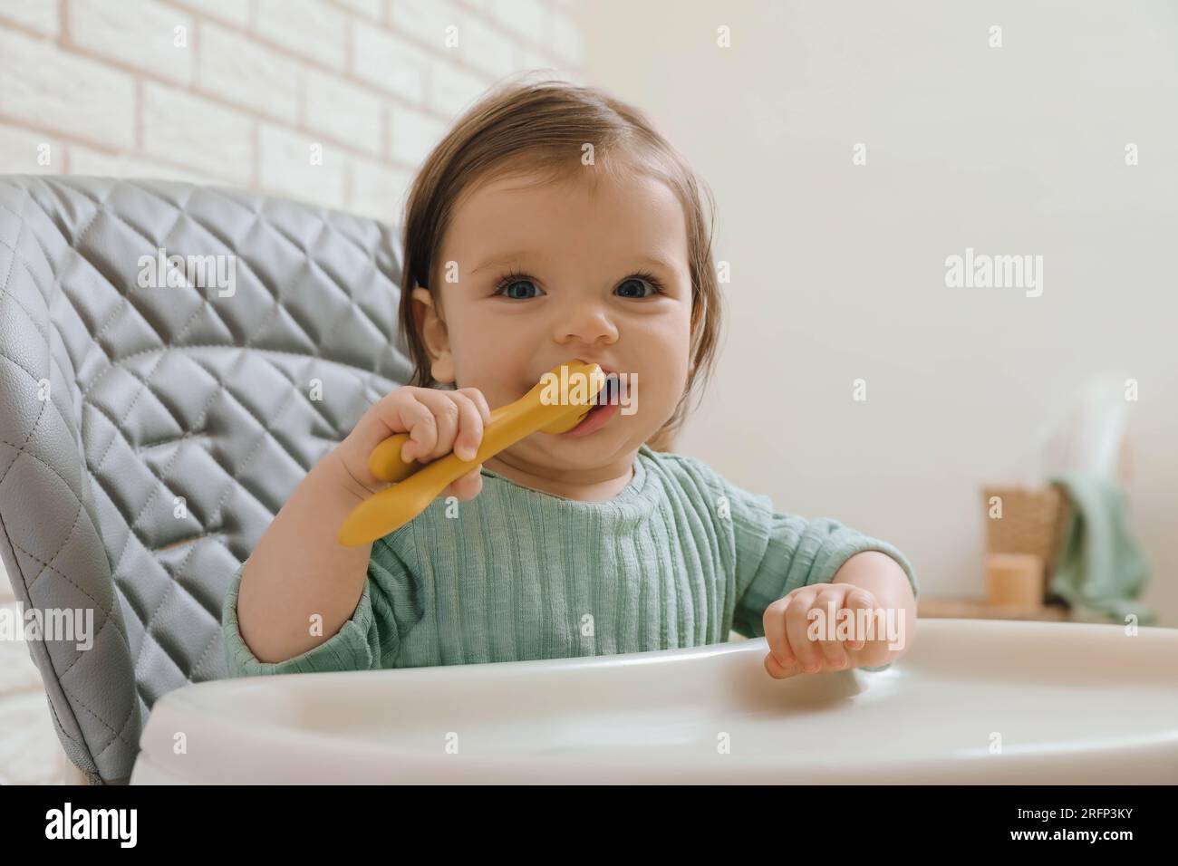 Cute little baby nibbling cutlery in high chair indoors Stock Photo - Alamy