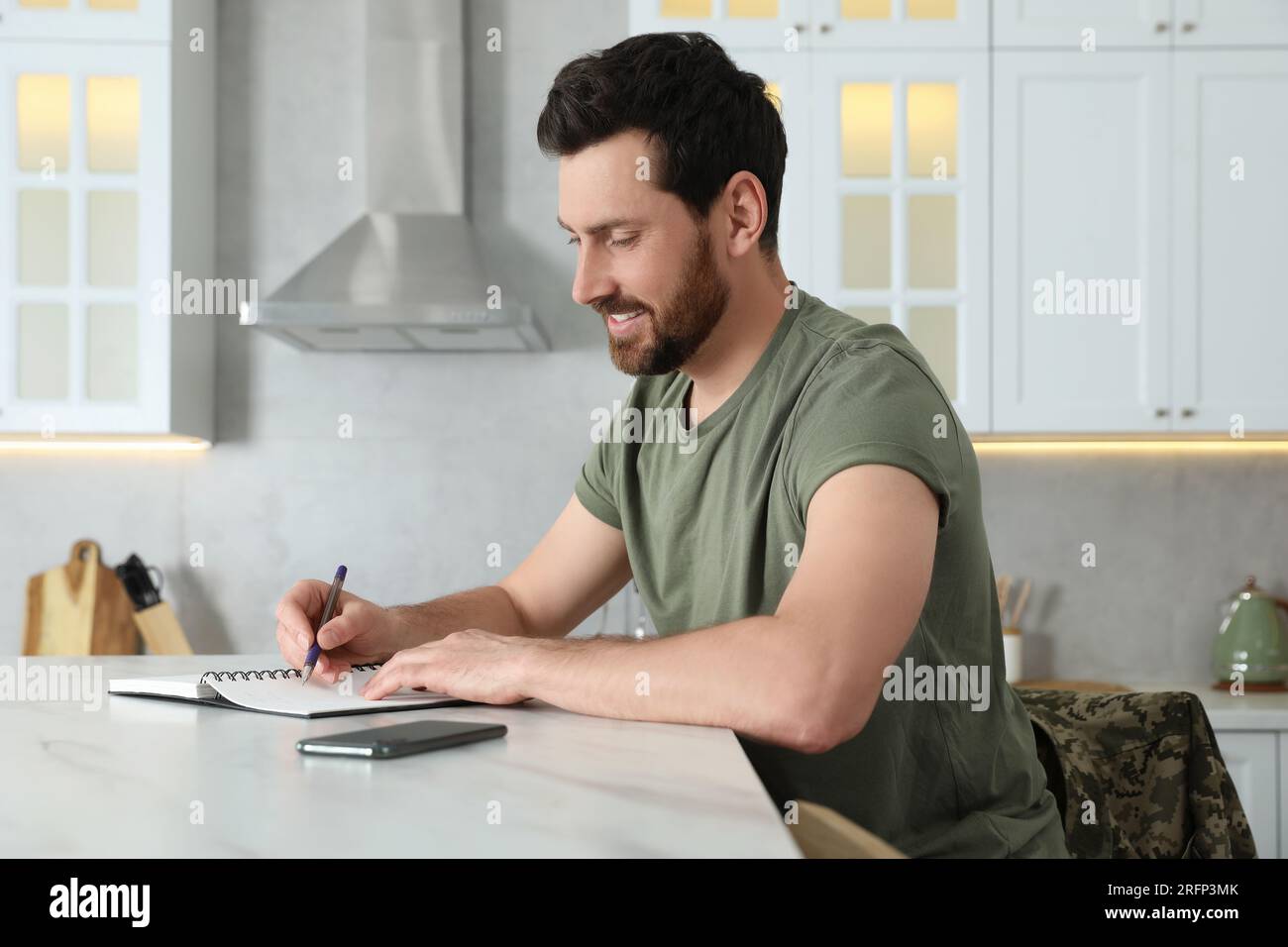 Soldier writing in notebook at white marble table in kitchen. Military ...