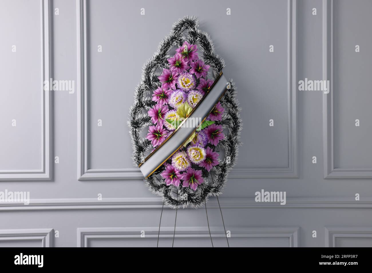 Funeral wreath of plastic flowers with ribbon near light grey wall ...