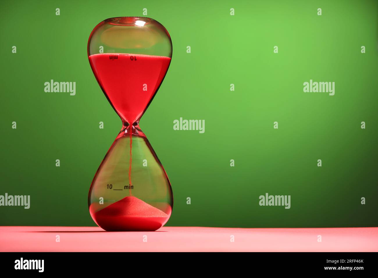 Hourglass with red flowing sand on color background. Space for text ...