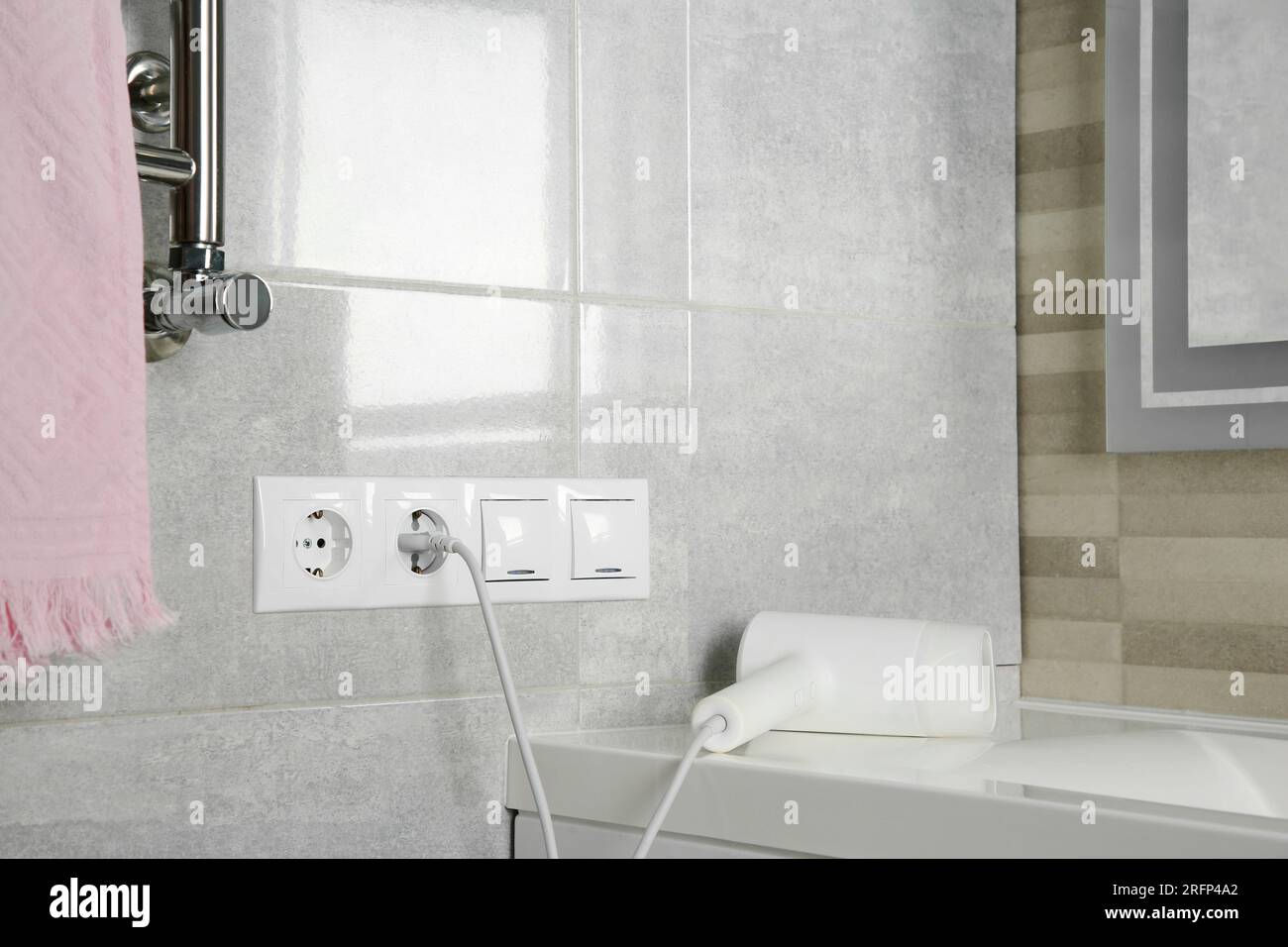 Hairdryer plugged into power socket on light grey wall in bathroom ...
