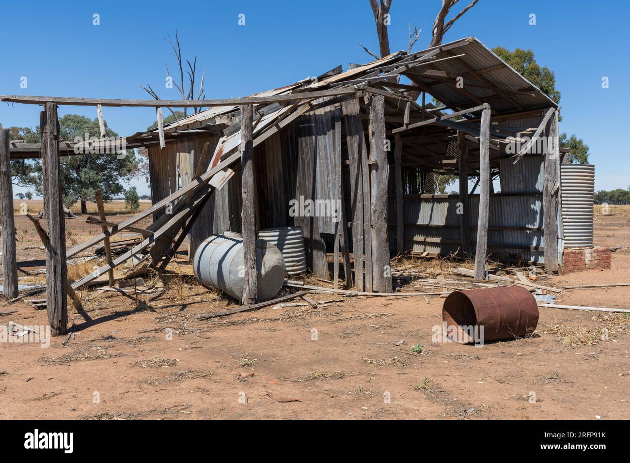 Ruins of an old farm shed with a corrugated tank under a clear blue sky ...