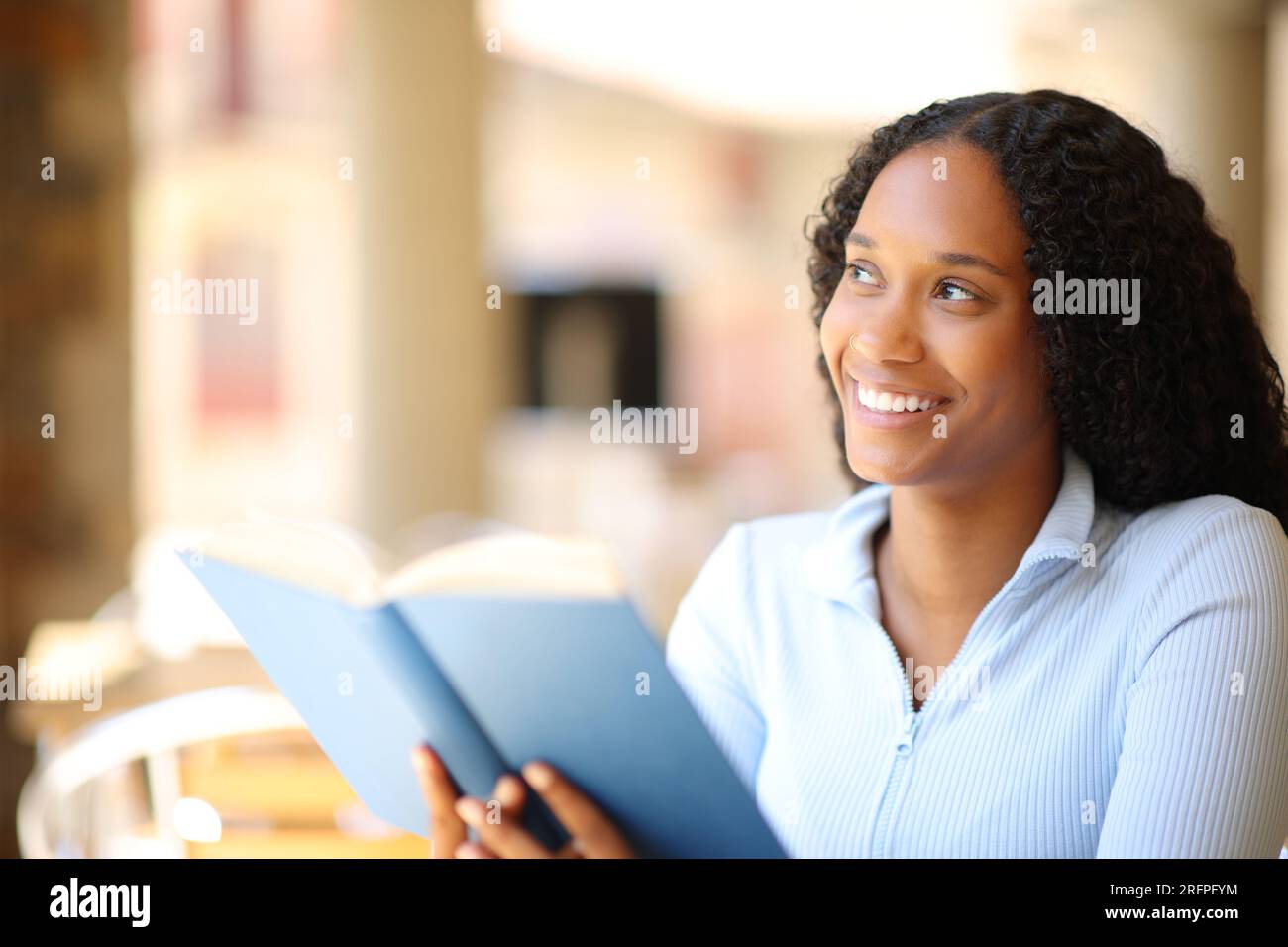 Happy black reader dreaming looking at side holding paper book in a ...
