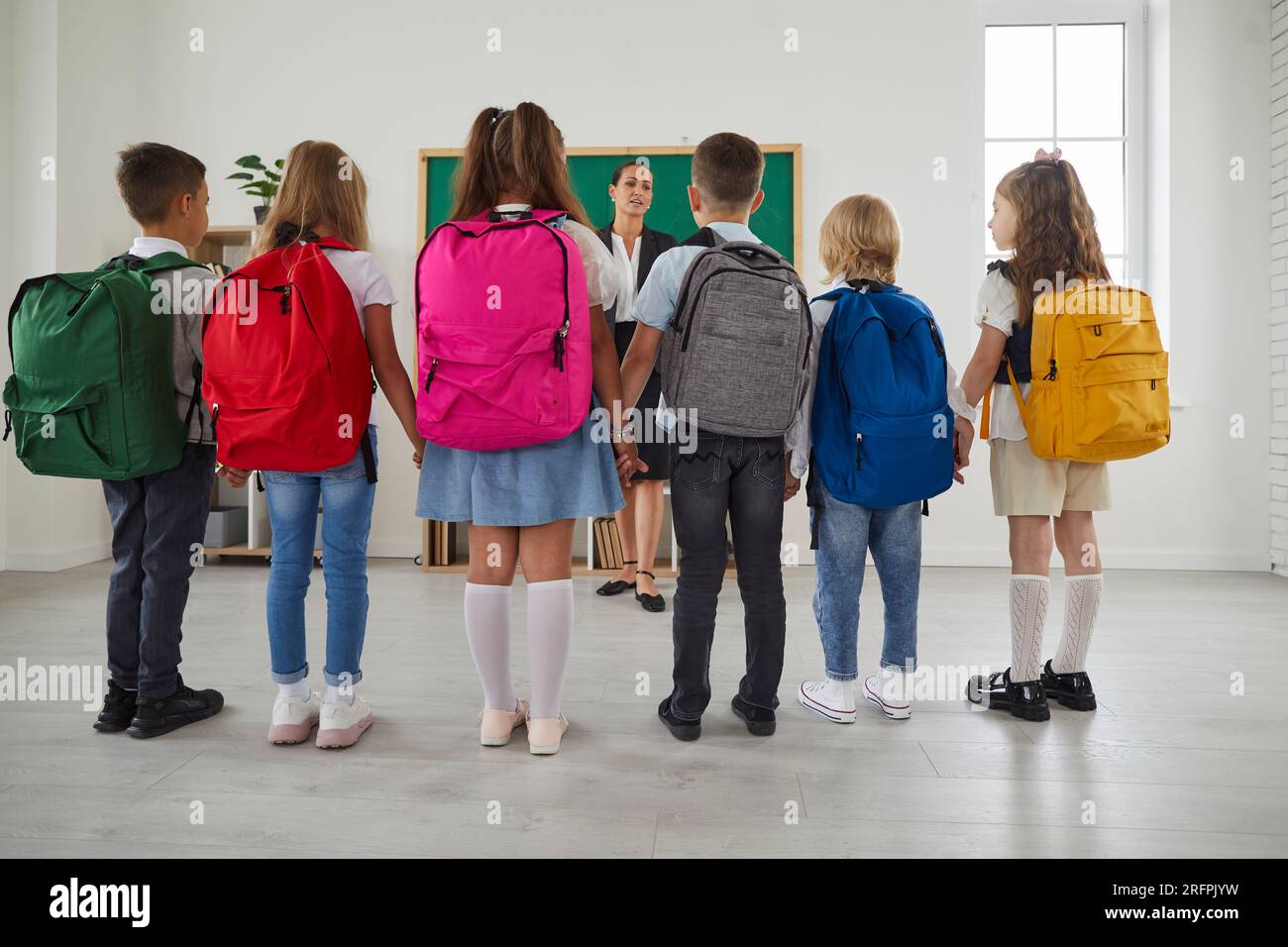 Group of classmates standing back around teacher at classroom before ...