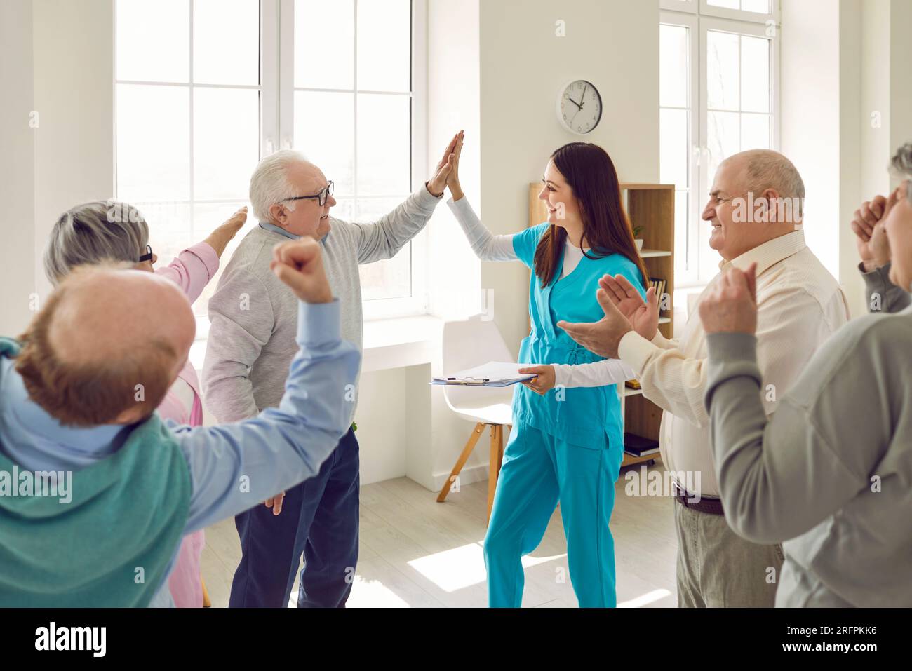 Senior man doing high five with a young friendly nurse in a group ...
