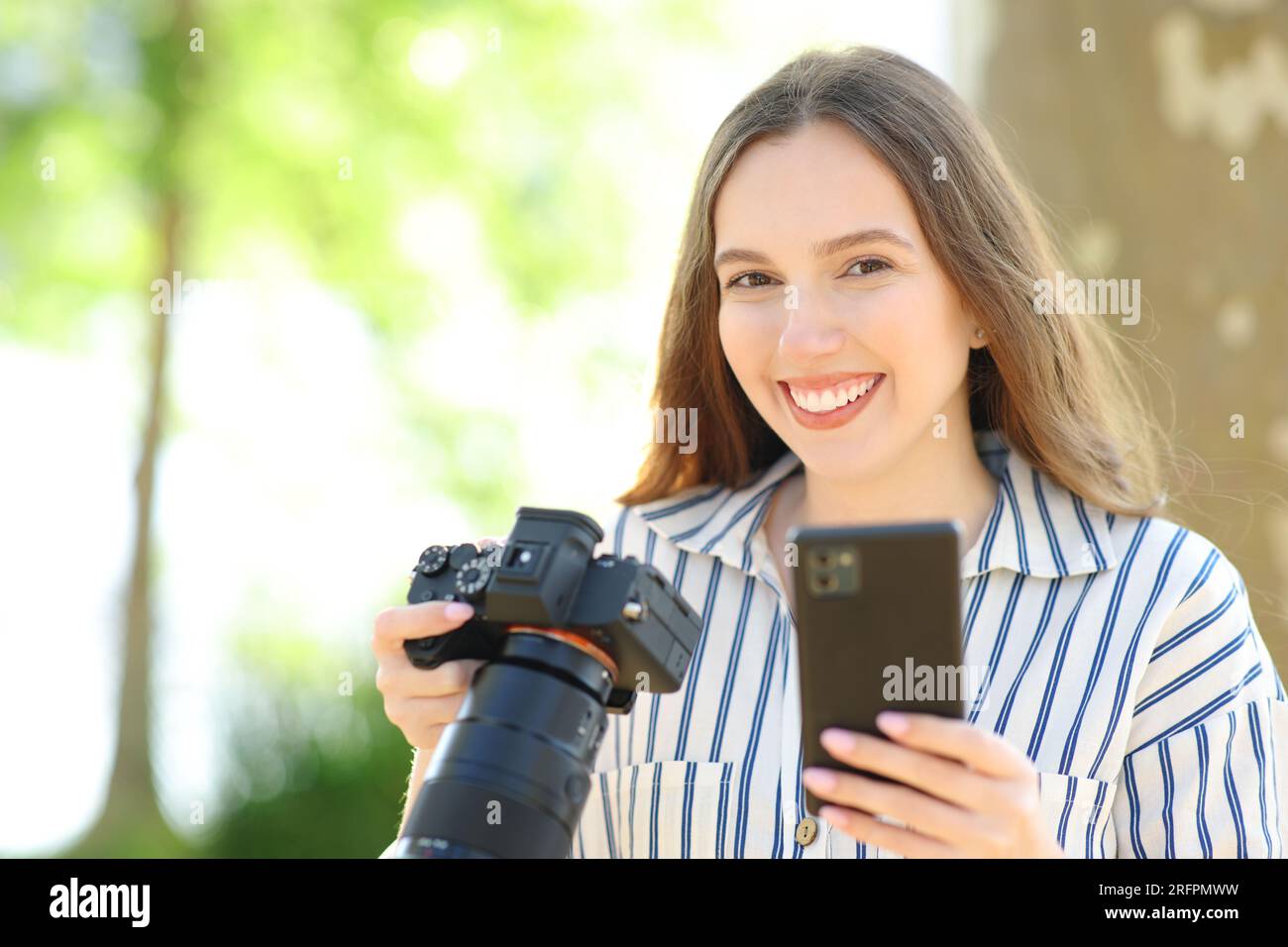 Happy photographer holds camera and smart phone posing looking at you in nature Stock Photo - Alamy