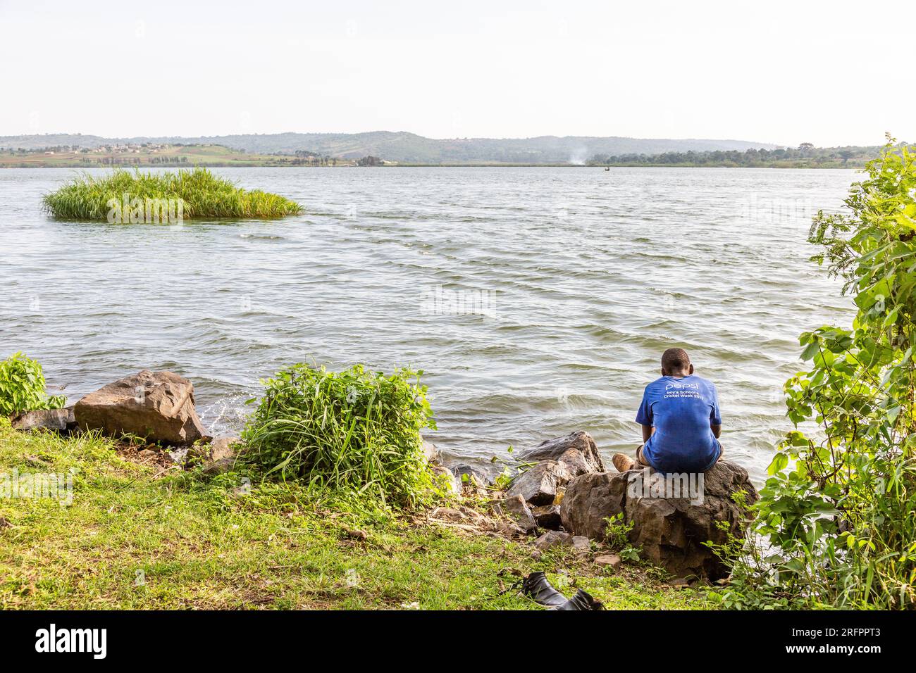 Person sitting on a stone on the edge of Lake Victoria, where its ...